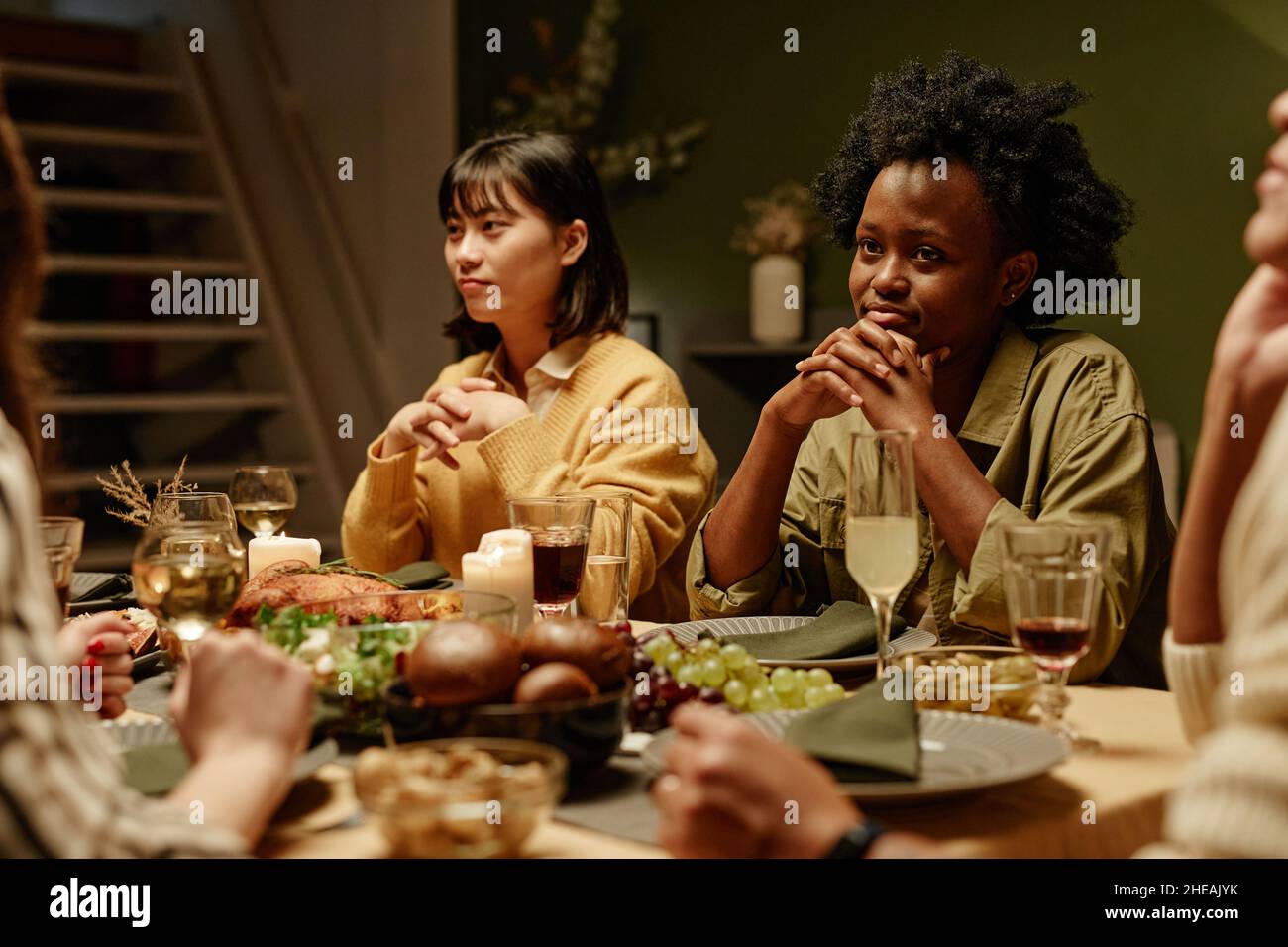 Young women sitting at dining table and listening to friends while they ...