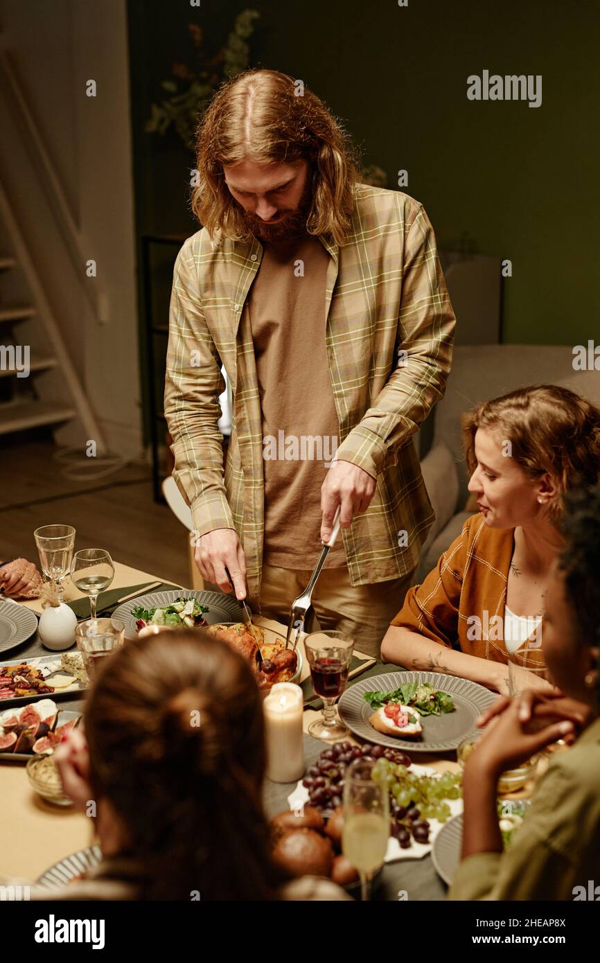Young man cutting turkey with knife at dining table and serving it to ...
