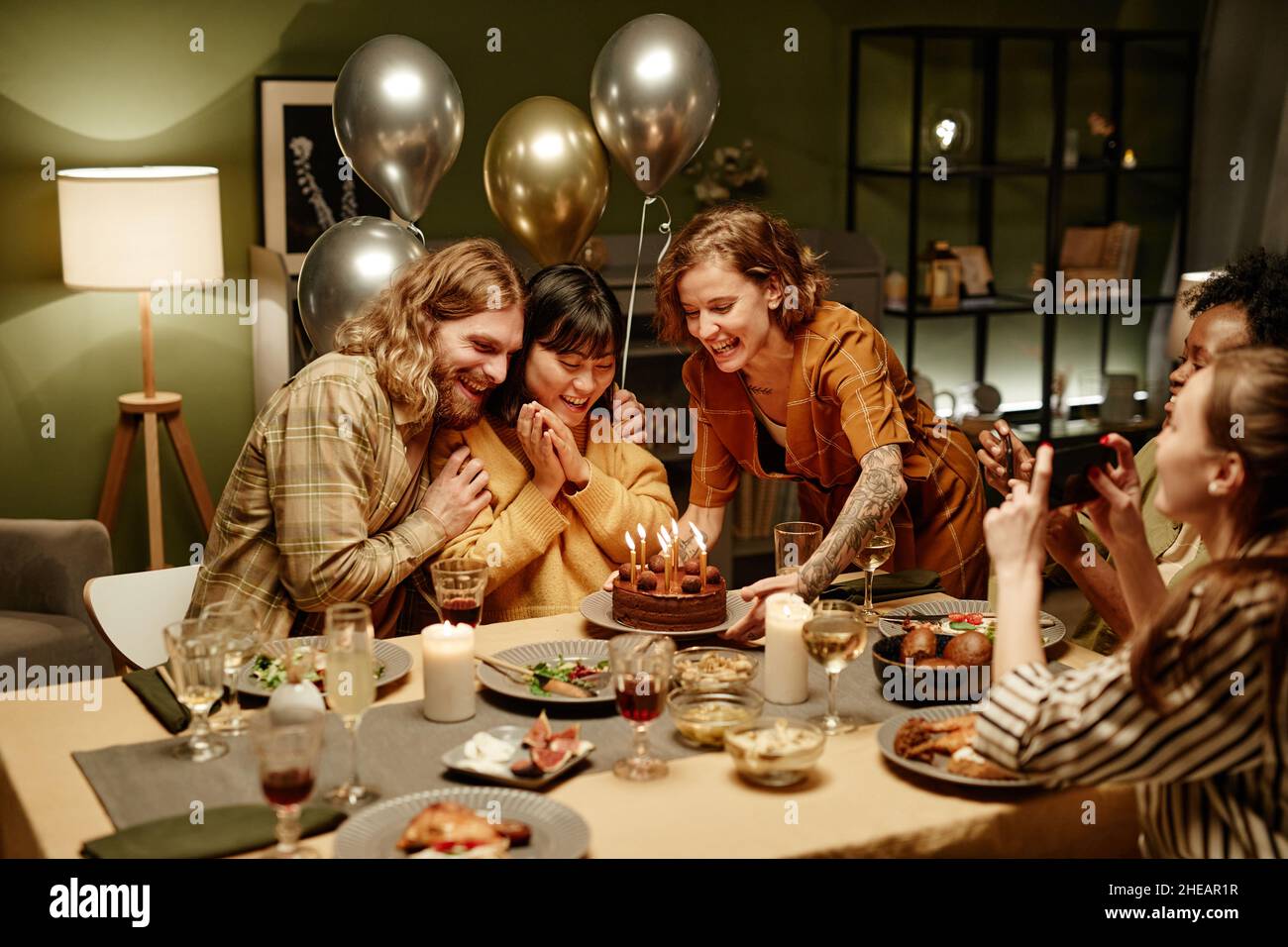 Happy young woman celebrating birthday with her friends at home, they ...