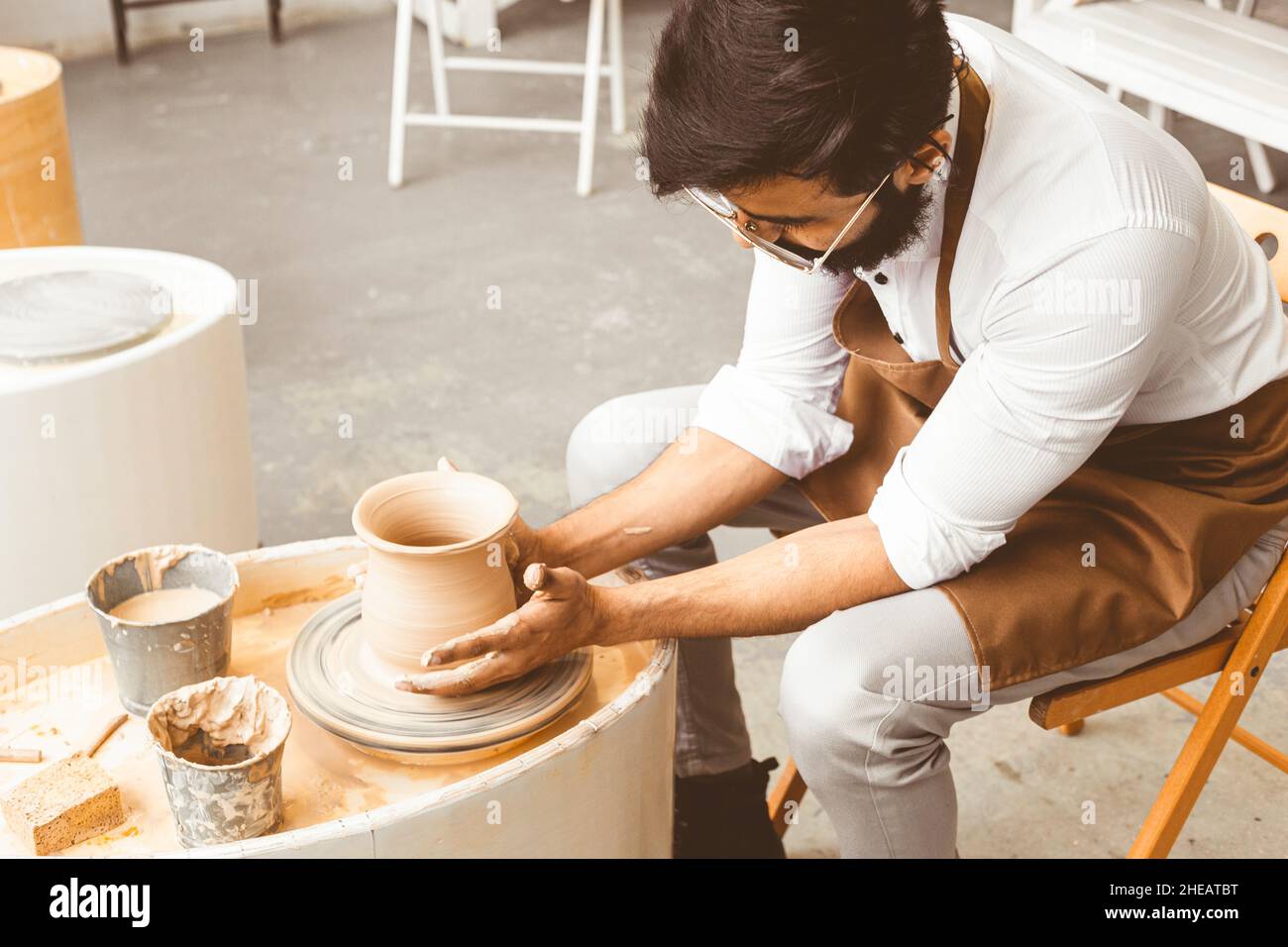 A young male potter is engaged in craft in his workshop on a potter's ...