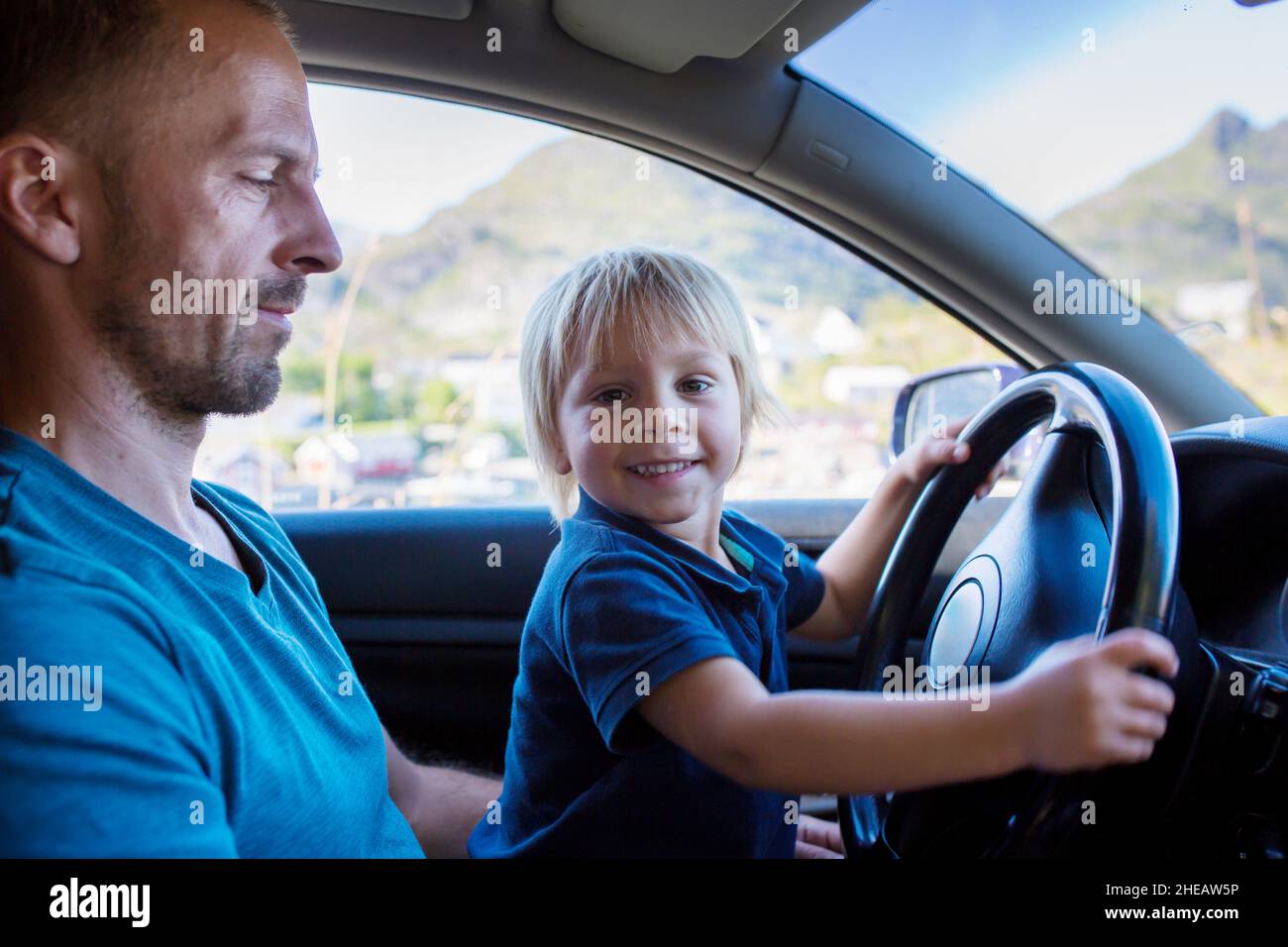 Toddler child, boz, sitting in fathers lap and pretending to drive a ...