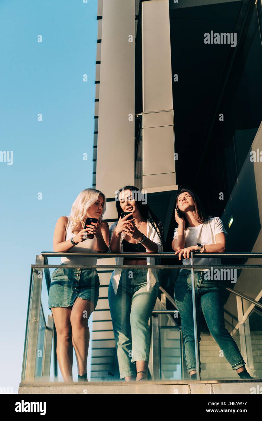 Three female friends using their mobile phones while hanging out ...