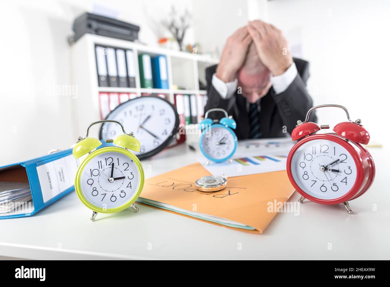 Stressed businessman behind his desk full of alarm clocks Stock Photo - Alamy