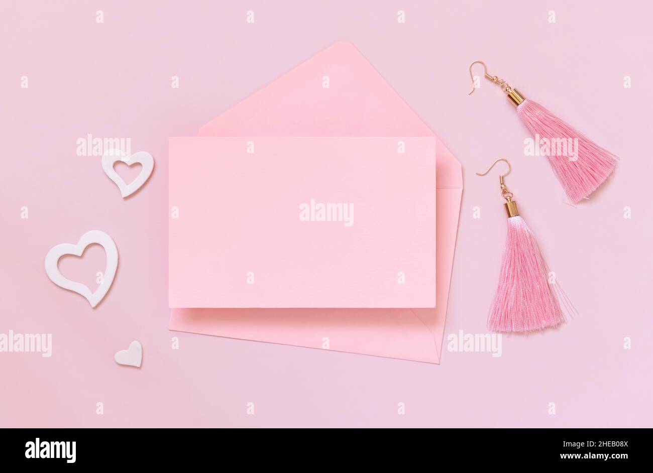 Pink paper card and envelope, hearts and tassel earrings on pink top ...