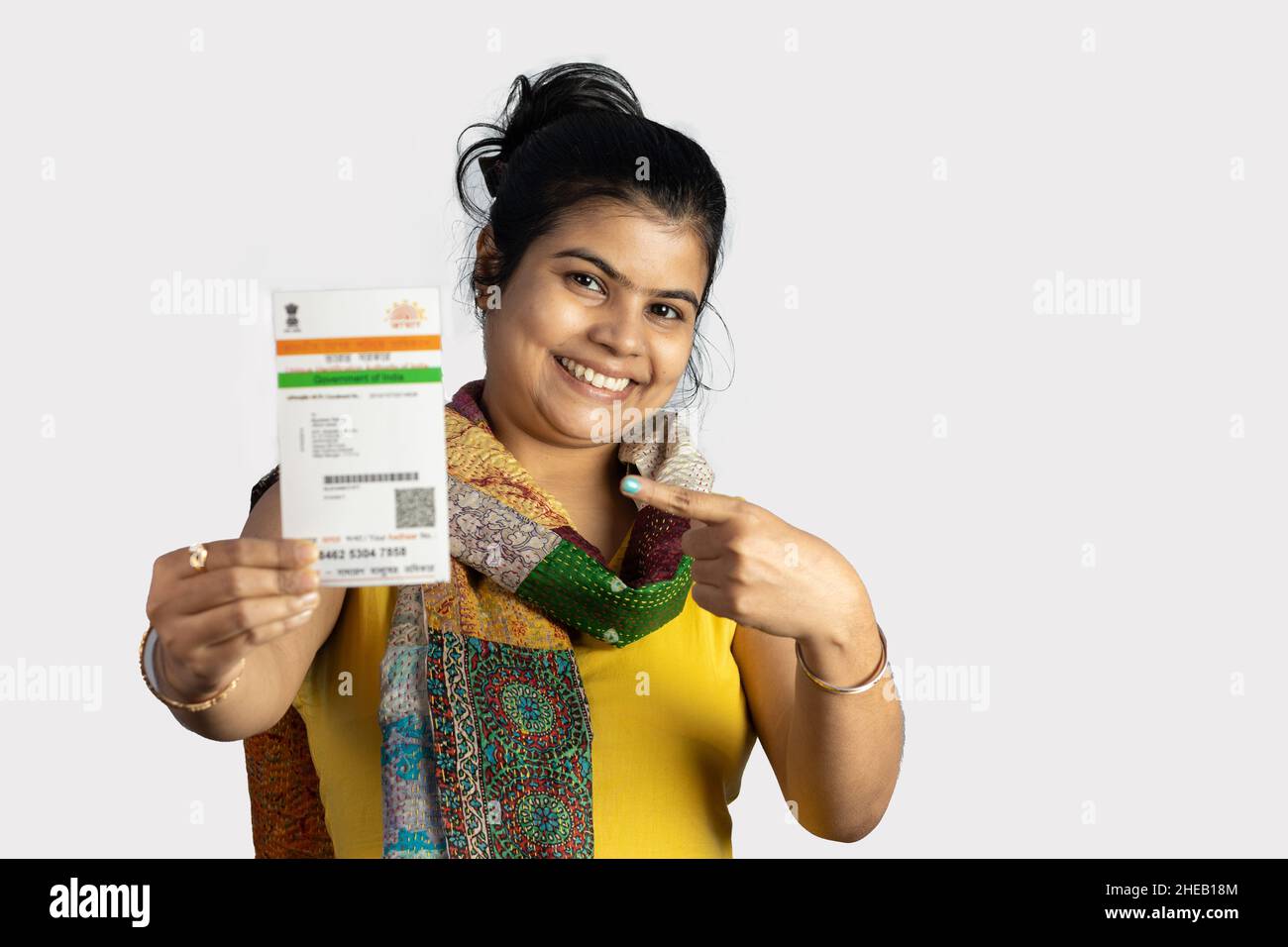 An Indian young woman smiling and pointing to Aadhaar card in hand on ...