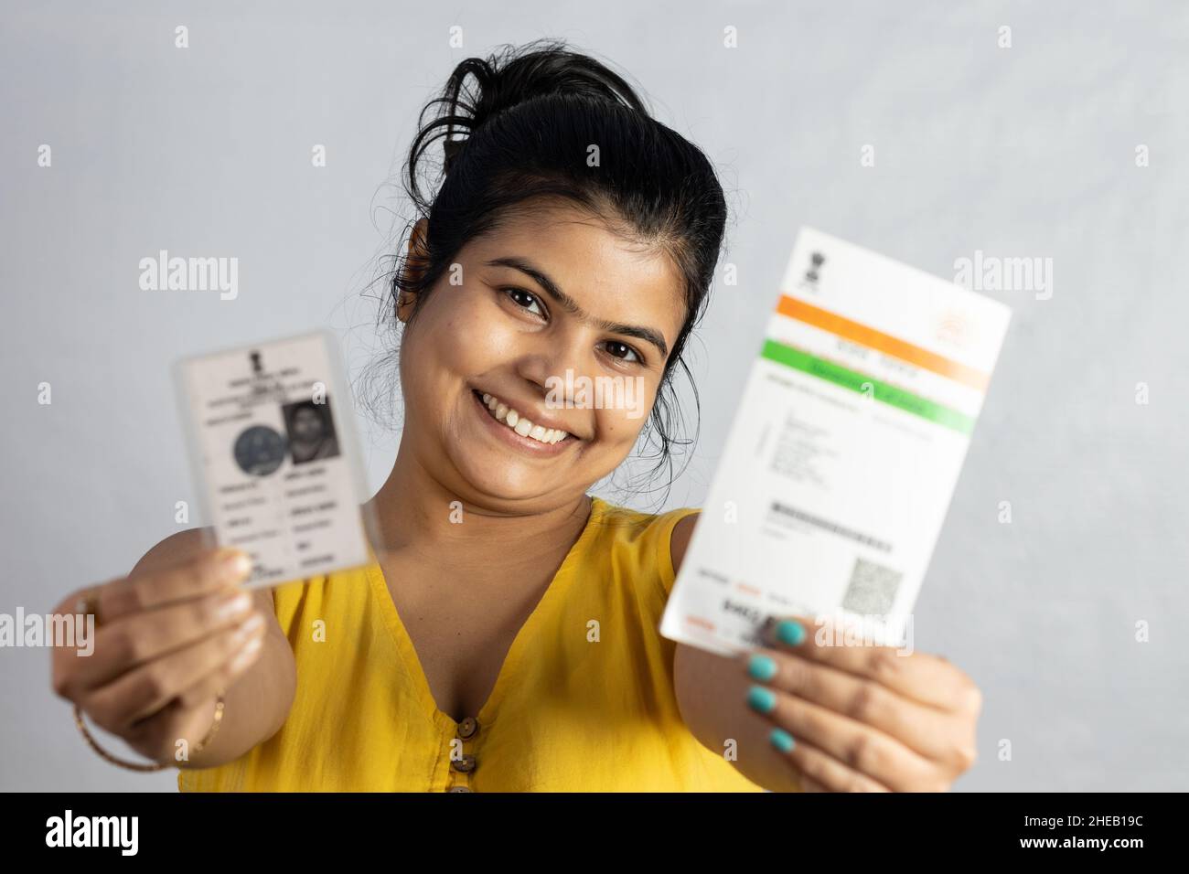 An Indian young woman smiling with Aadhaar card and voter card in hands ...