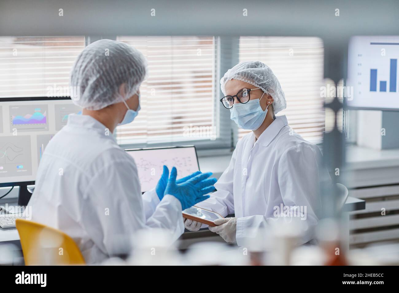 Two scientists in protective workwear talking to each other during ...