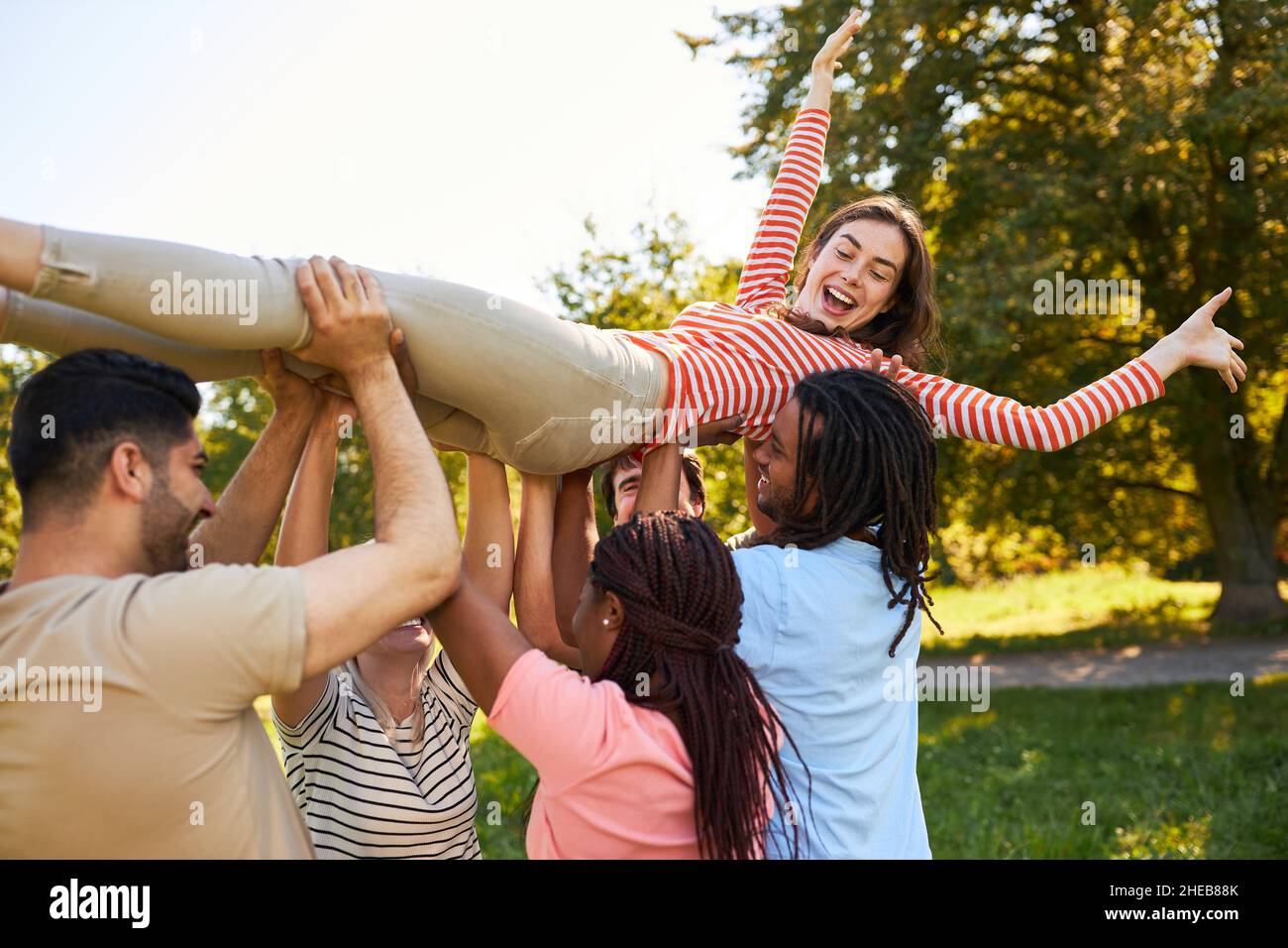 Group of multicultural people carries young woman together during a ...