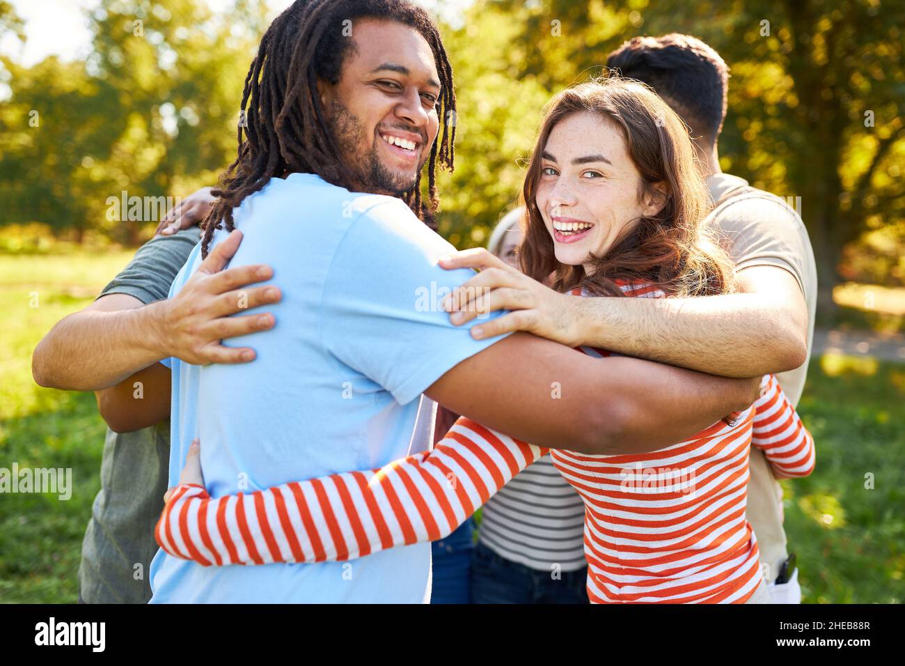 Group of young people stand hugging in a circle as a community in the ...