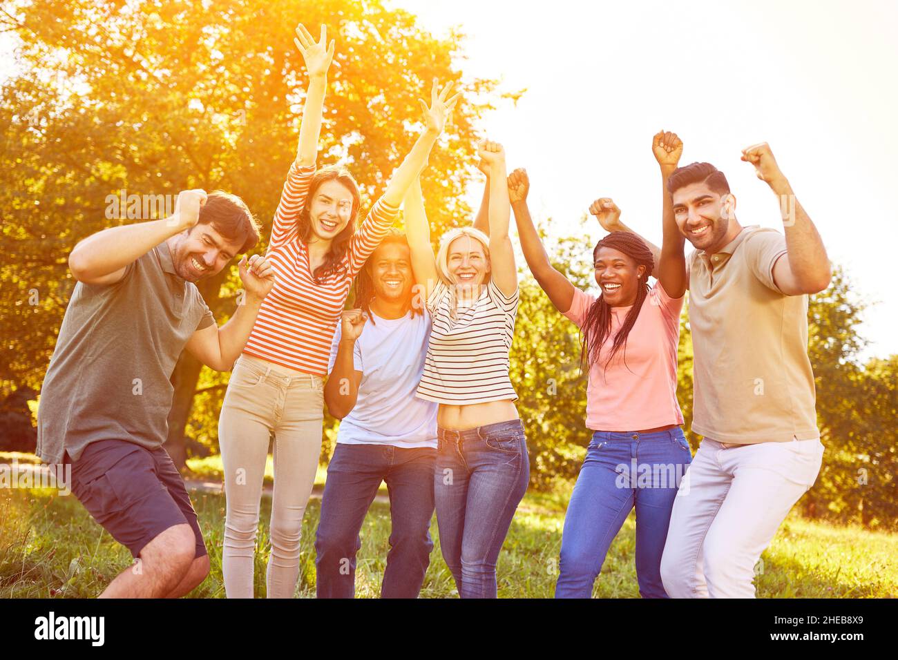 Happy group as a successful team cheers in the park at a team building ...