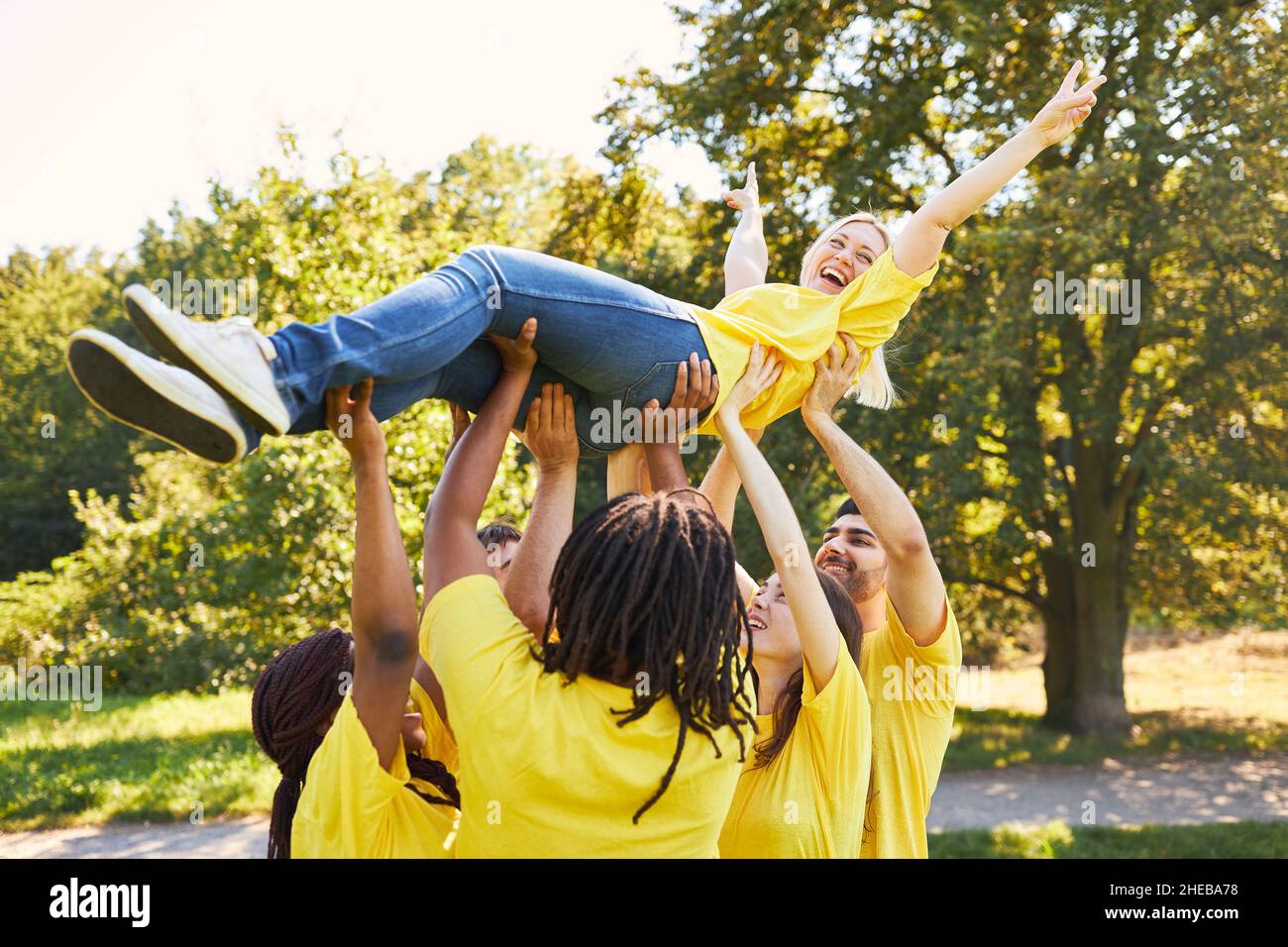 Group of young people together lifts woman up in team building workshop ...