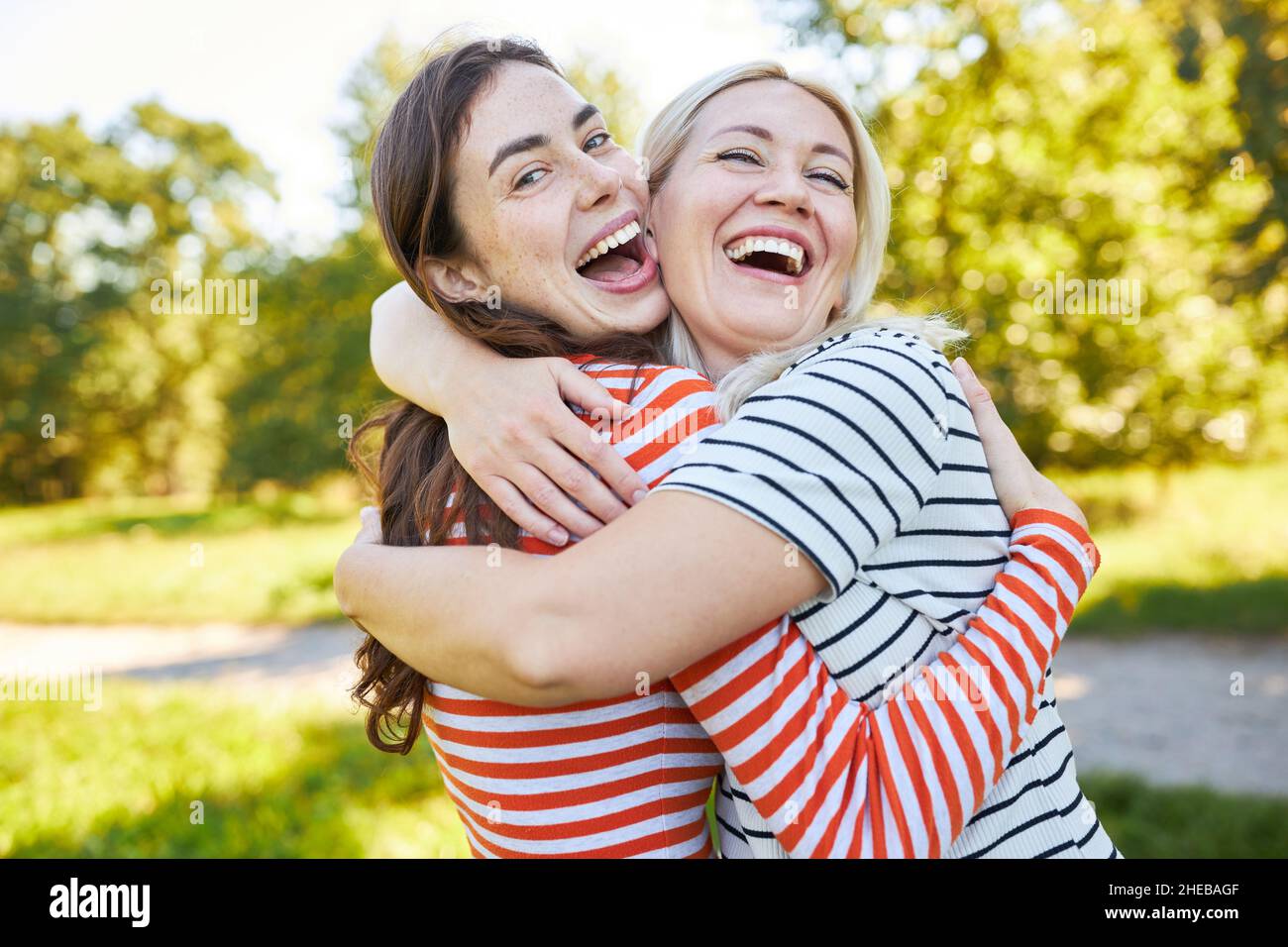Two laughing girlfriends hug each other happily in nature in summer ...