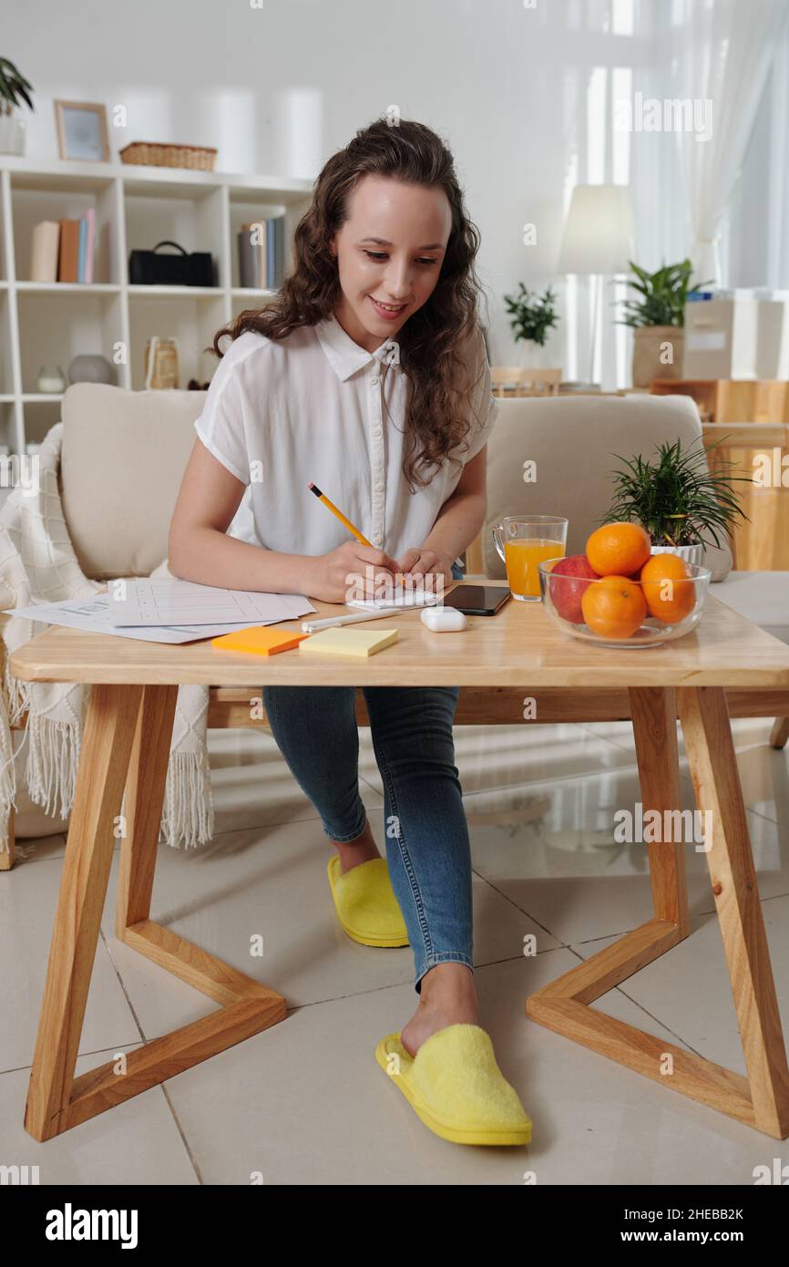 Smiling young project manager working from home, writing down ideas ...