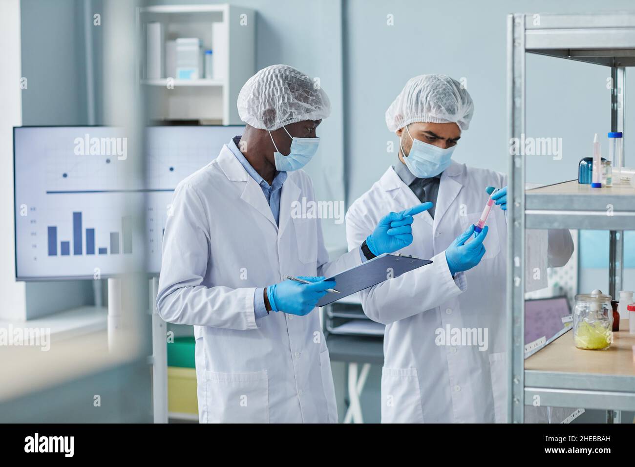 Two scientists in lab coats examining analysis in test tubes and making ...