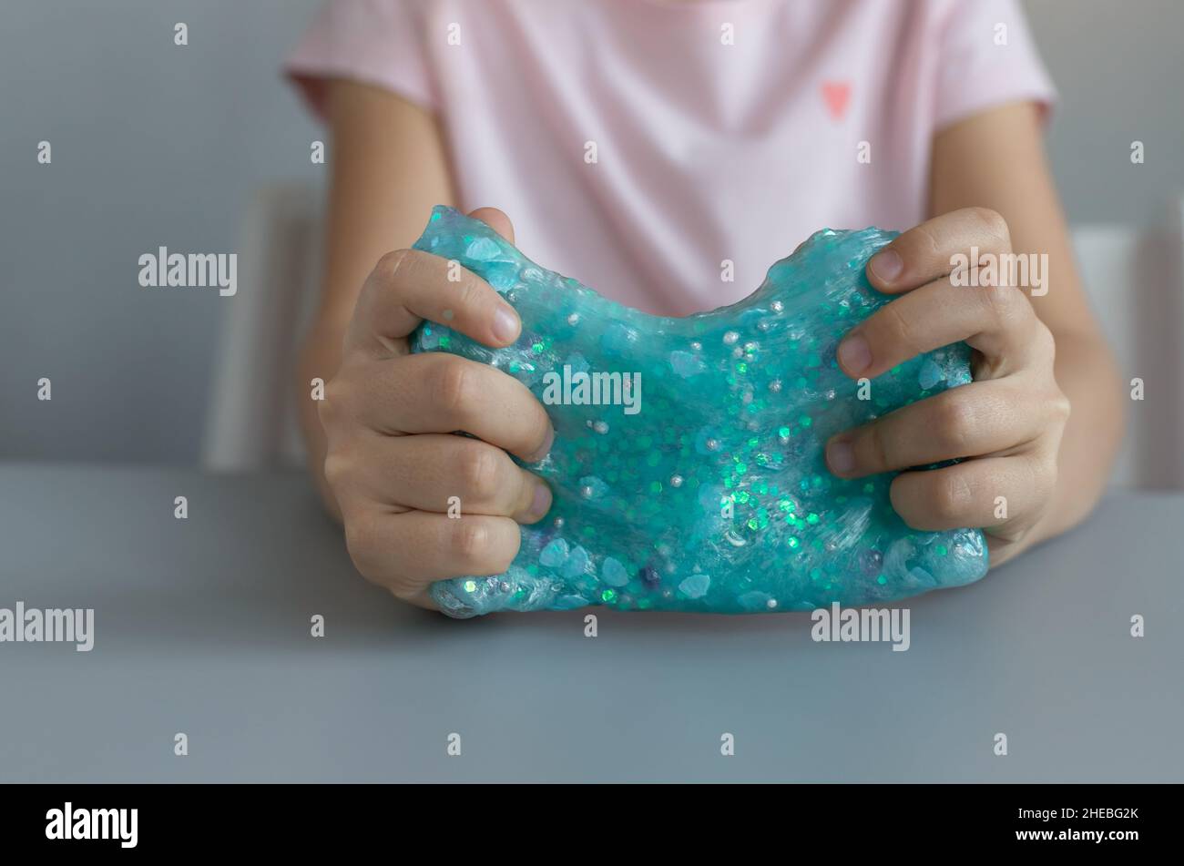 preschooler girl sitting at desk and playing with blue slime Stock ...