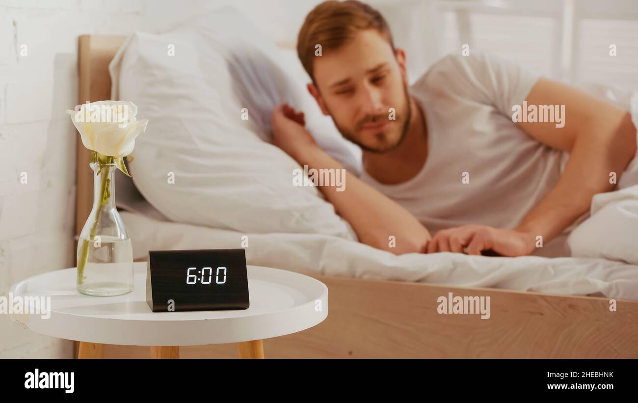 Clock and flower on bedside table near blurred man on bed at home Stock ...