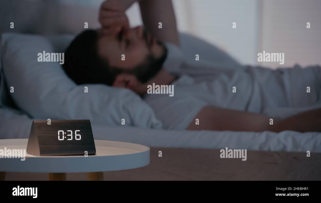 Clock on bedside table near blurred man in bedroom at night Stock Photo ...