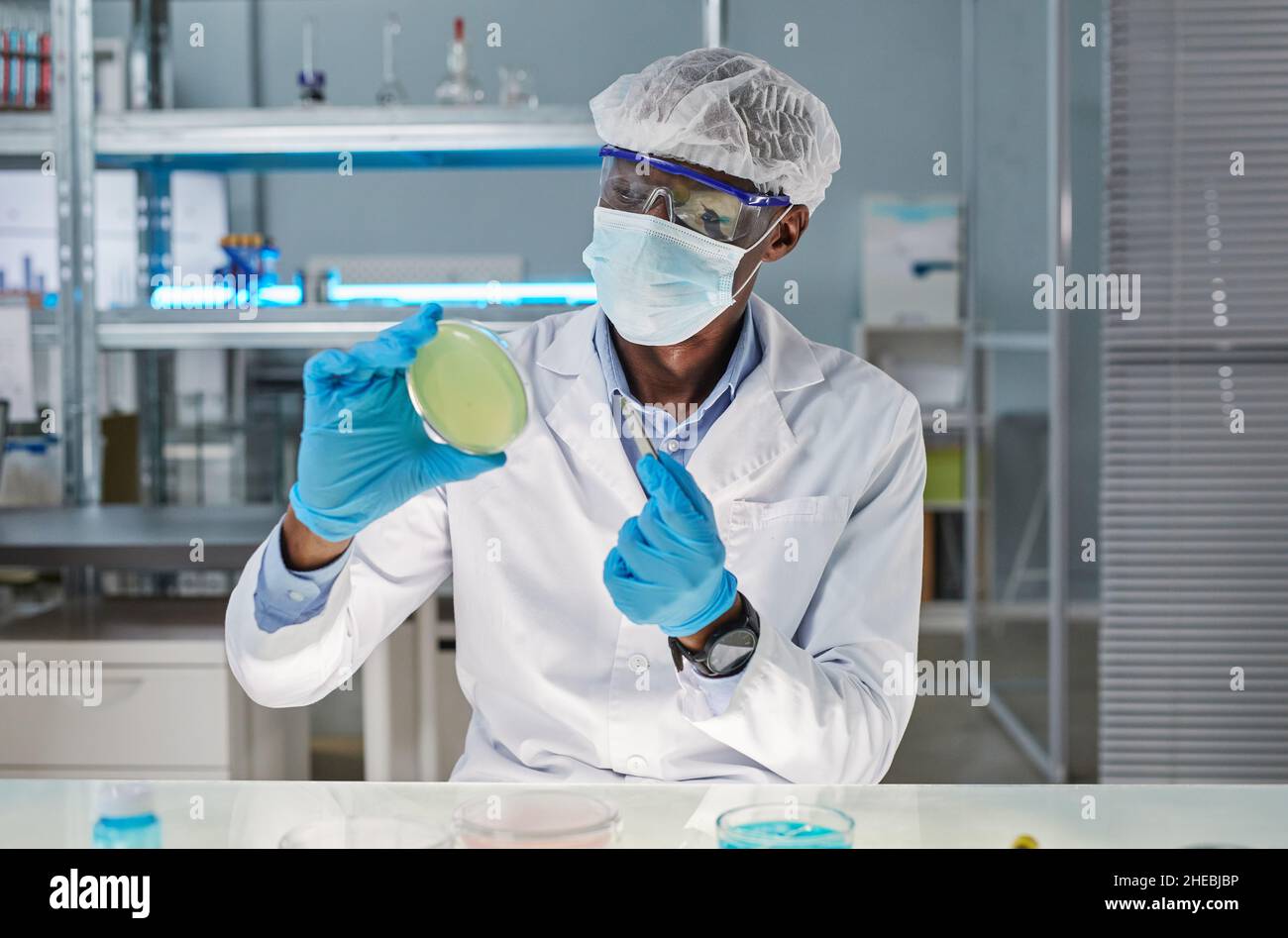 African young scientist in protective wear taking sample during ...