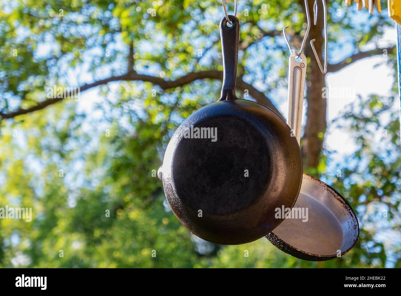 old frying pans hanging and drying outside against the blue sky and ...