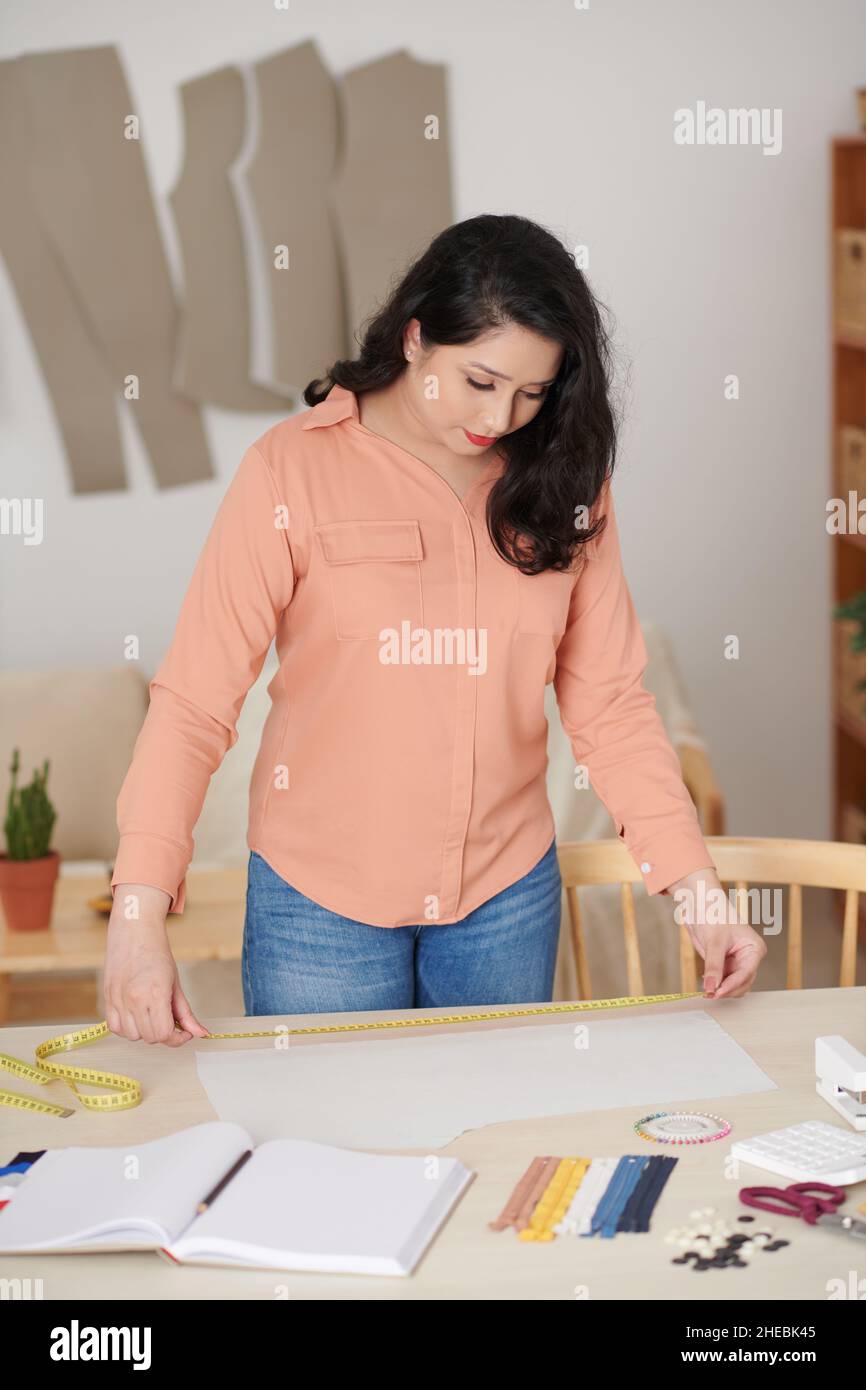 Seamstress measuring cut out sewing pattern on table in her workshop ...