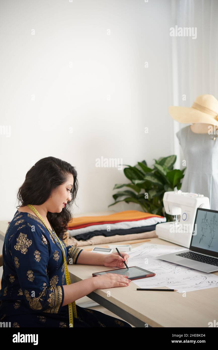 Talented creative tailor drawing fashion sketches on tablet computer ...