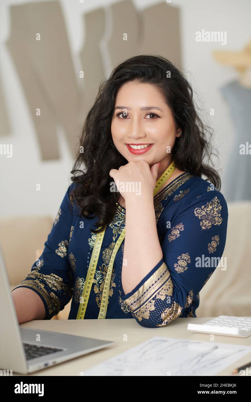 Portrait of cheerful Indian tailor in traditional dress working on ...