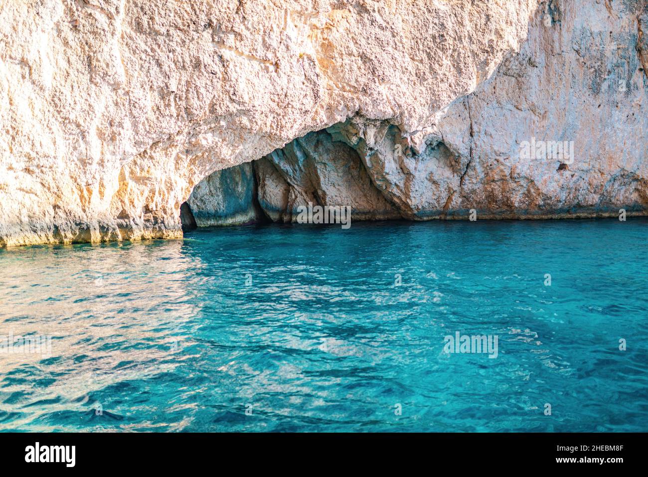 Layered light-colored rocks creating dark cave in sea beach of Corfu ...