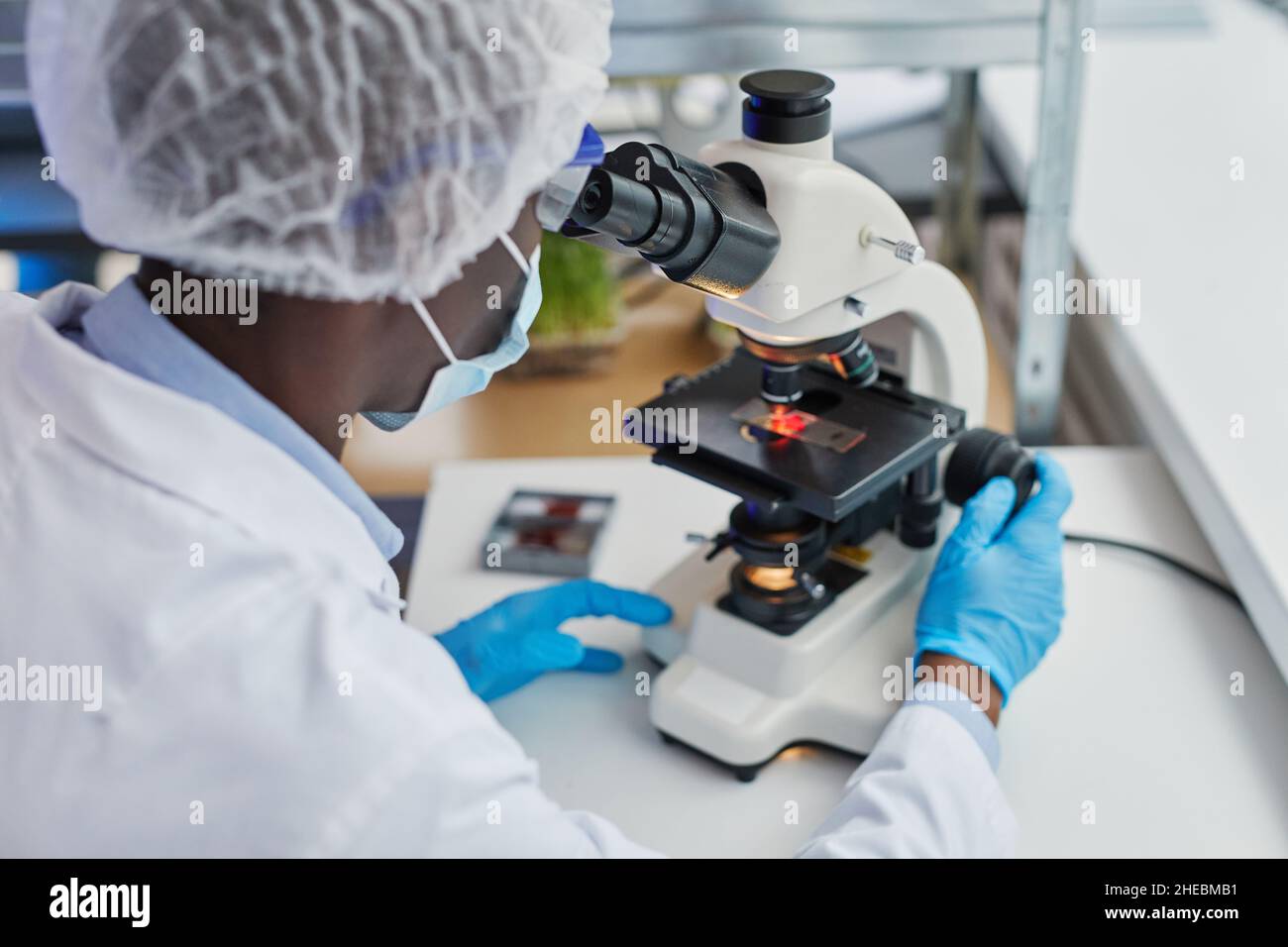 Rear view of African doctor looking through the microscope at the table ...