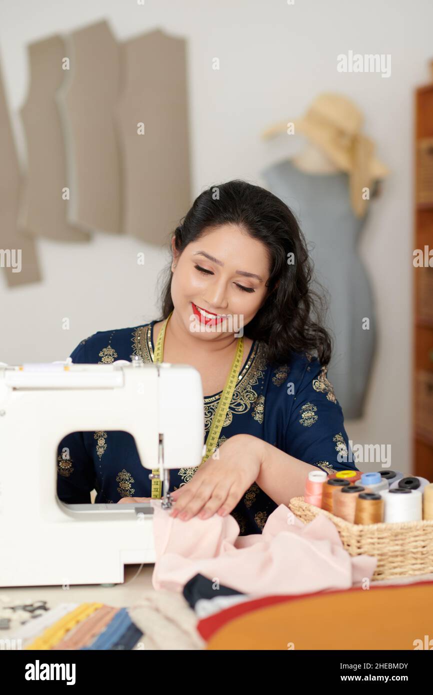 Portrait of smiling seamstress working on sewing machine in atelier ...