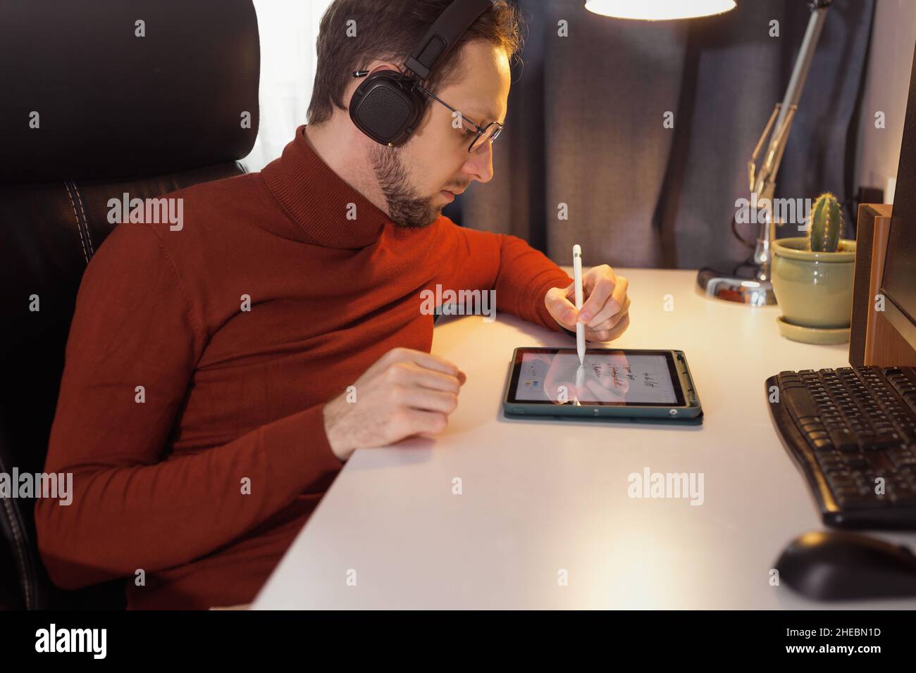 man in headphones works at home, takes notes in an electronic tablet ...