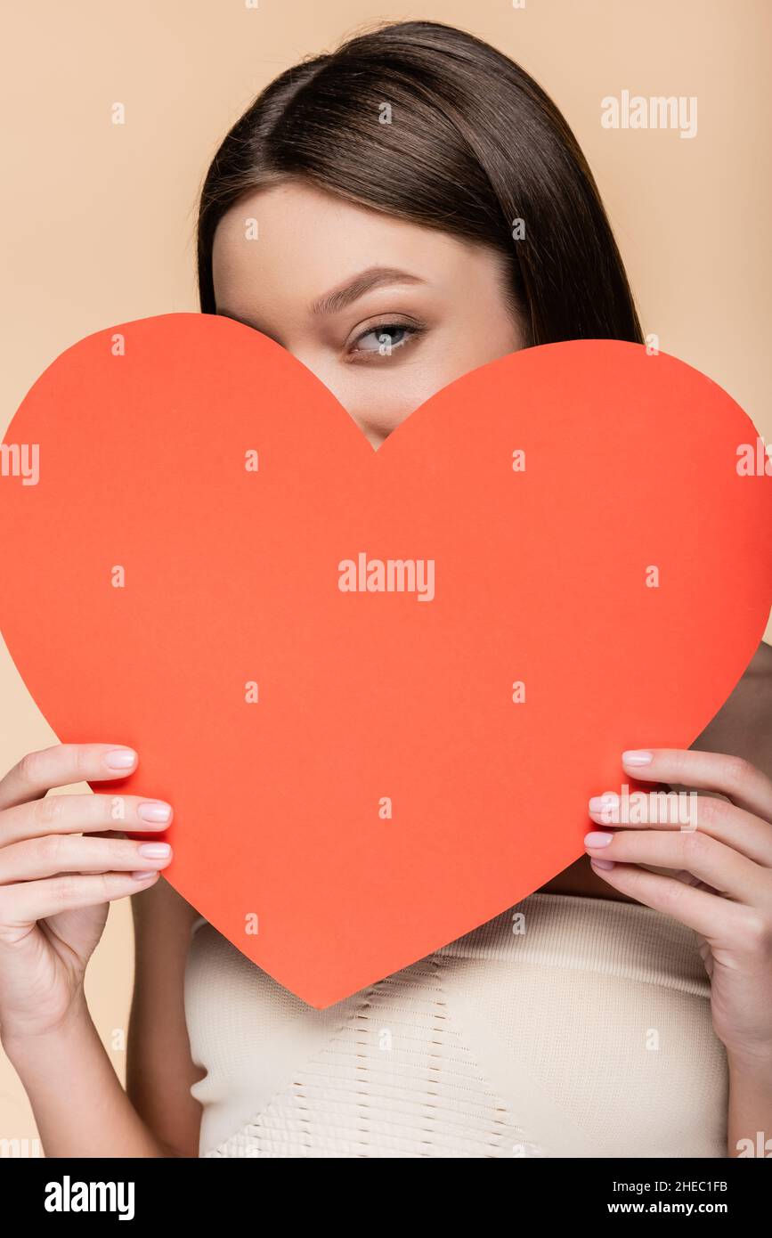 young woman covering face with red paper cut heart isolated on beige ...