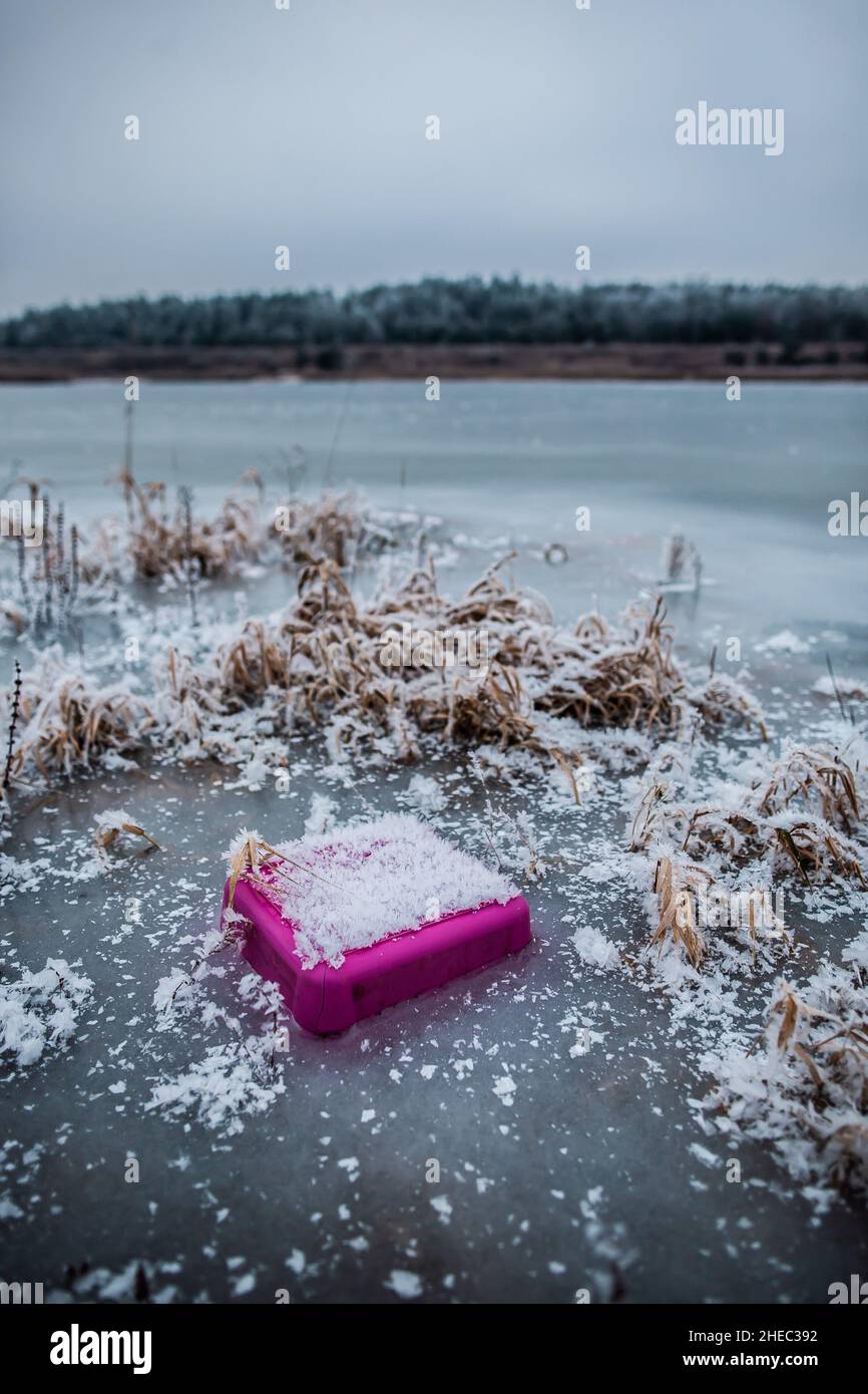 Plastic trash in frozen water, Pink piece of plastic covered with snow ...