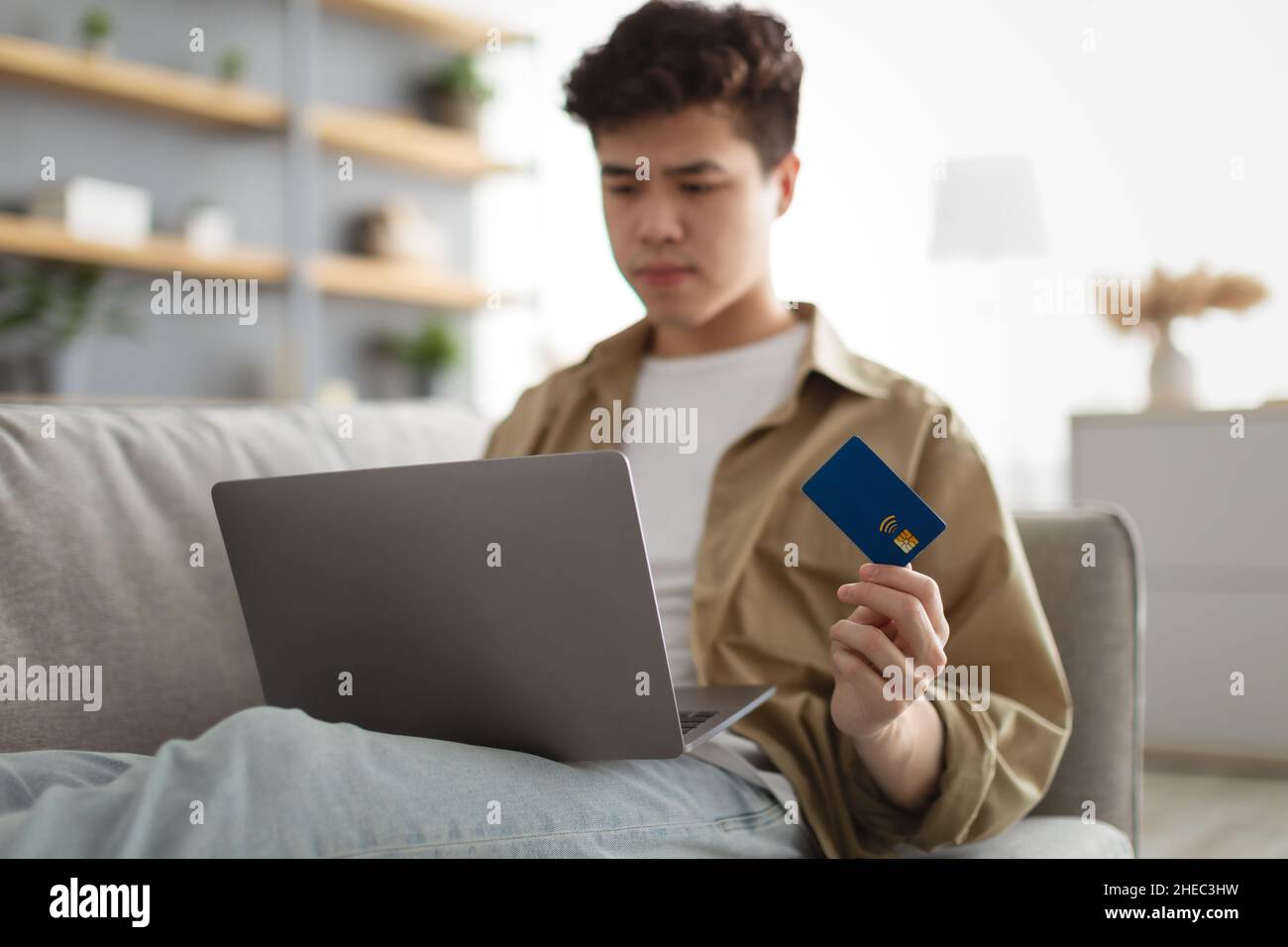 Focused asian guy showing using credit card at home Stock Photo - Alamy