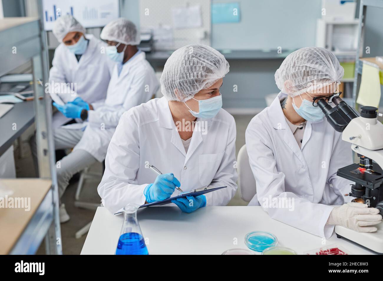 Young women in white lab coat making notes at the table while her ...