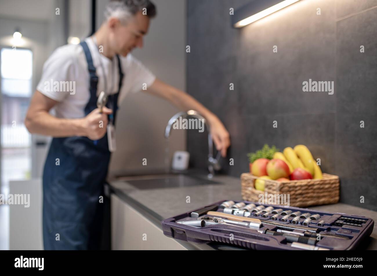 Set of tools on table and plumber opening tap behind Stock Photo - Alamy