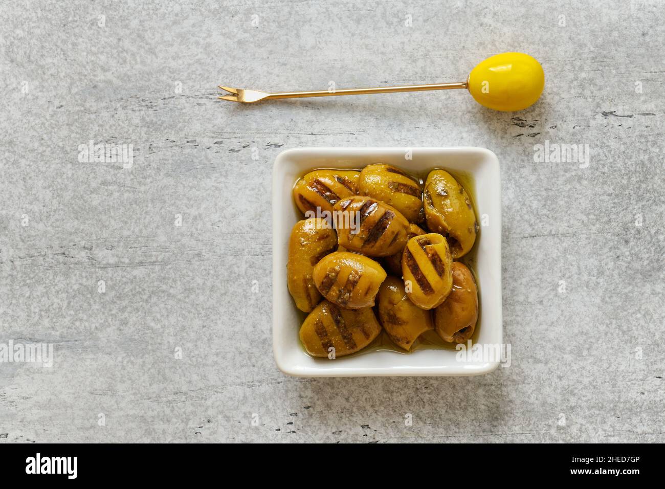 Grilled olives barbecued in olive oil with garlic in a square bowl and ...