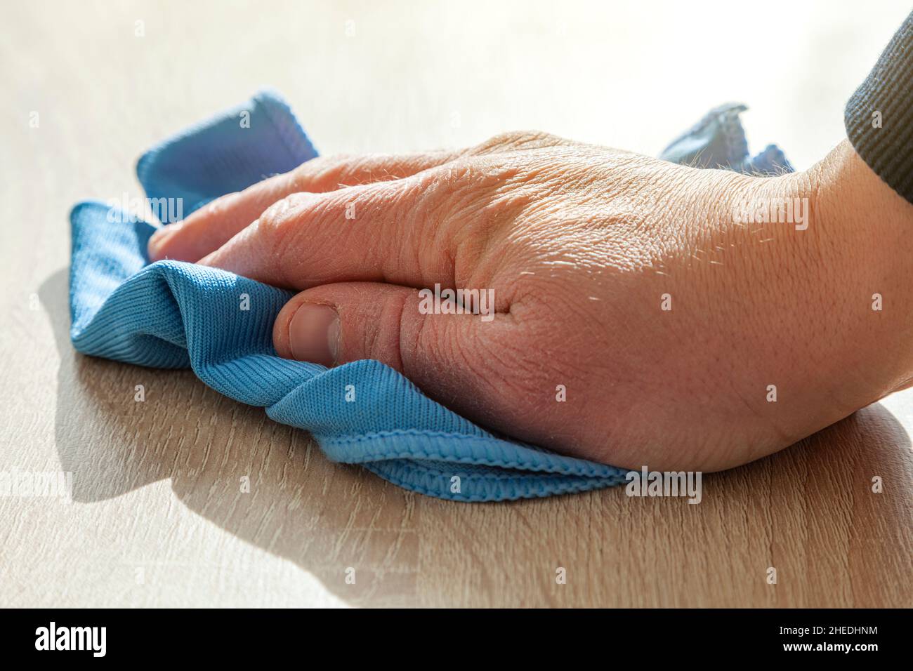 An older man's hand is wiping a wooden table with a blue cloth cloth ...