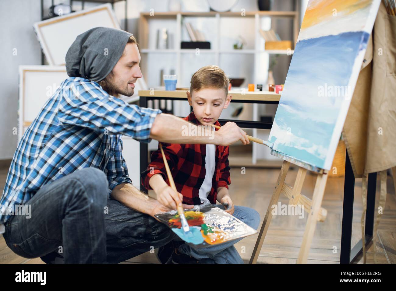 Qualified teacher and talented boy using brushes and color palette ...