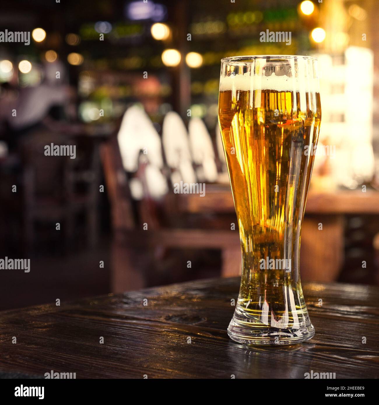 Glass of cold lager beer with foam on bar or pub desk. Blurred ...