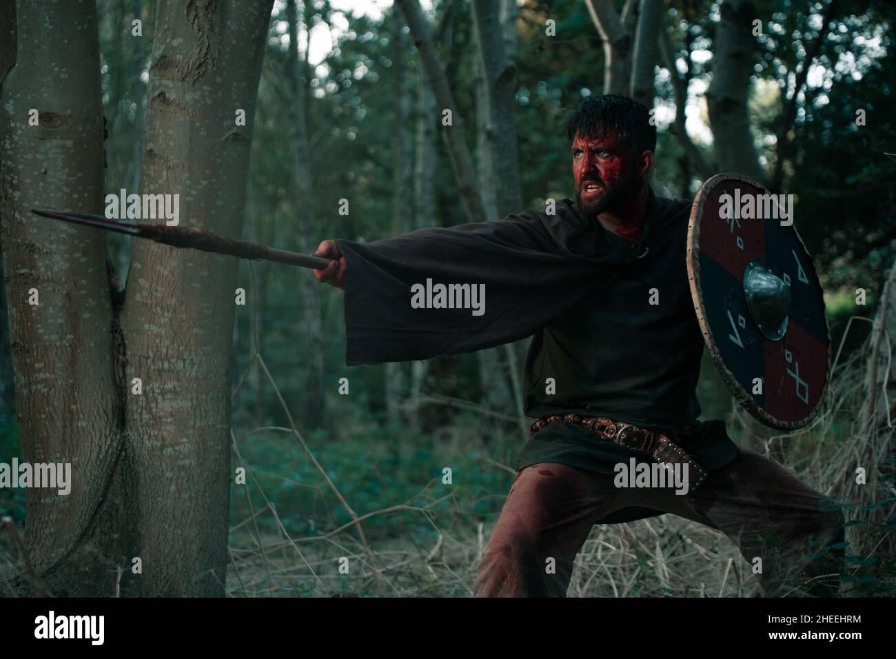 Angry male viking with face in blood fighting with spear and shield at ...