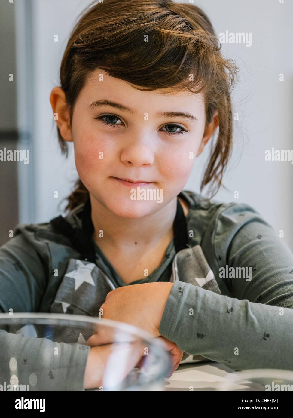 Cute little kid with brown hair and in gray apron standing in kitchen ...