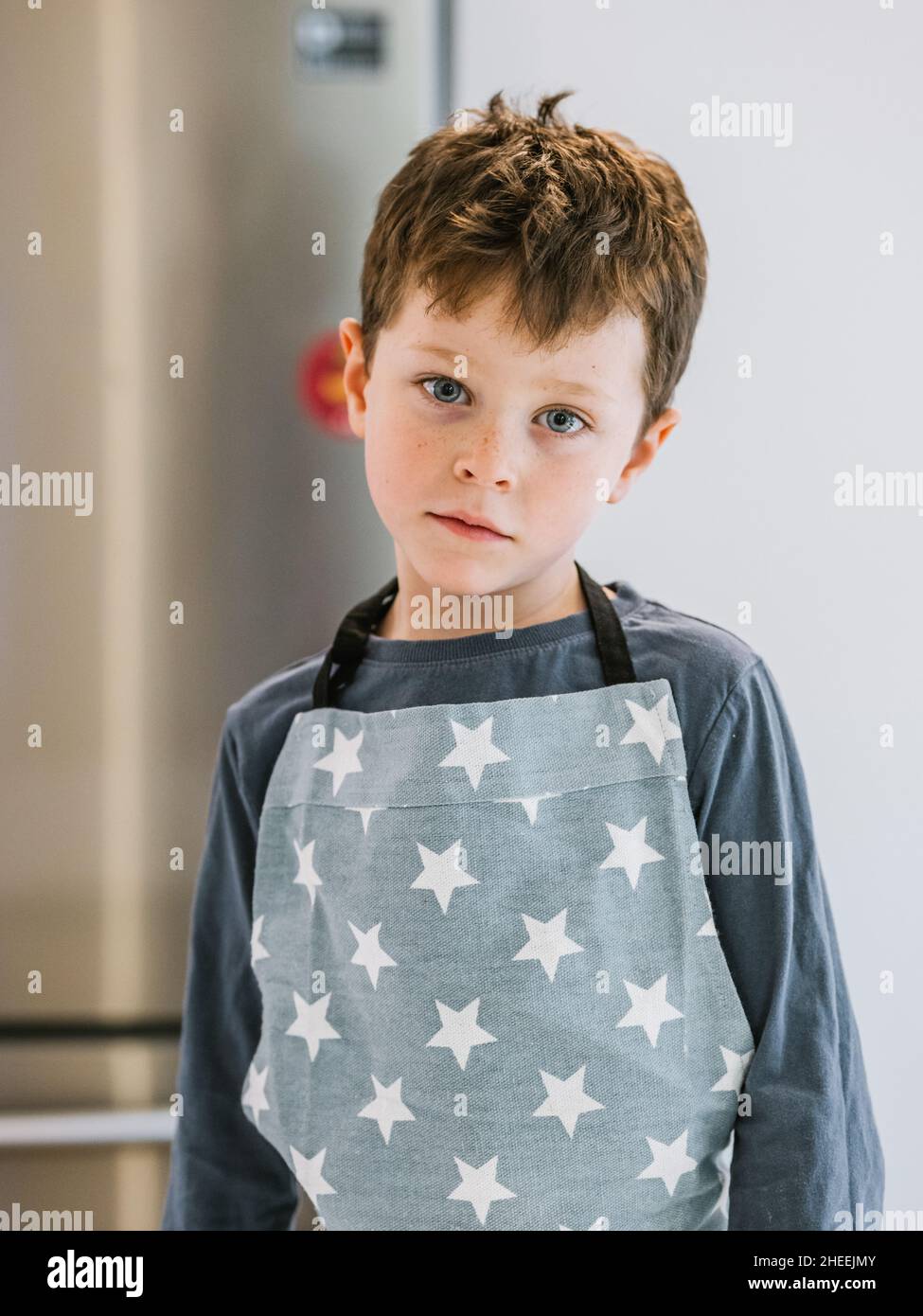 Cute little kid with brown hair and in gray apron standing in kitchen ...