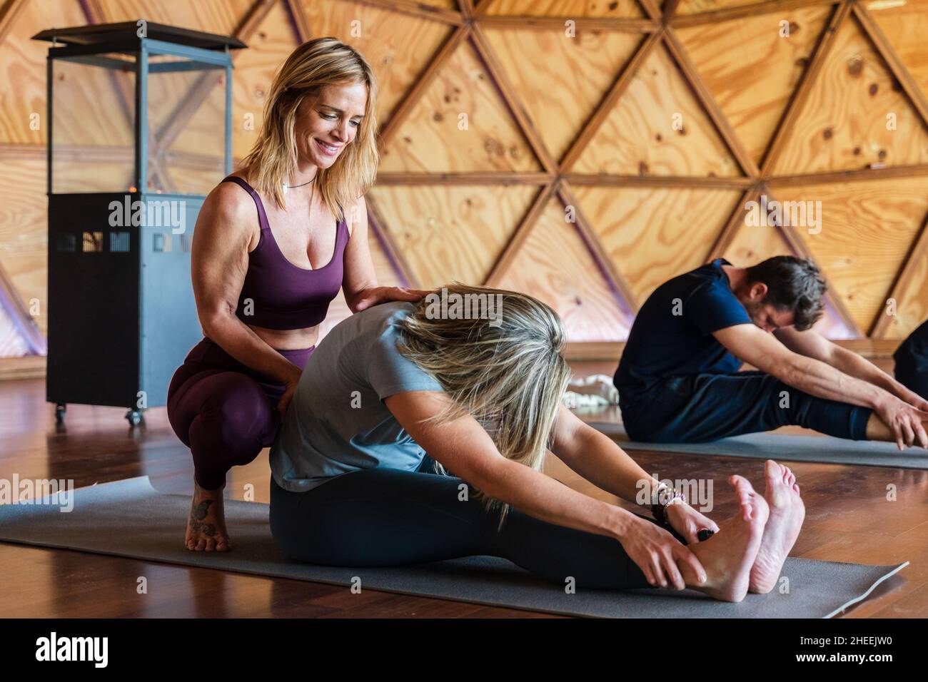Female trainer in sportswear helping active barefoot Woman on mat to do ...