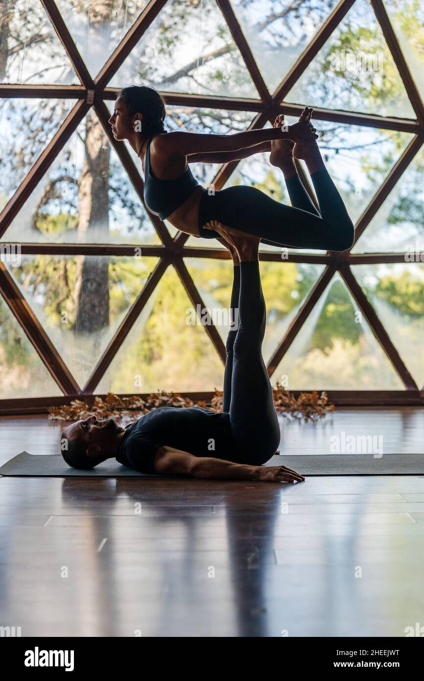 Full body side view of sporty couple in activewear performing bow pose during acro yoga session ...