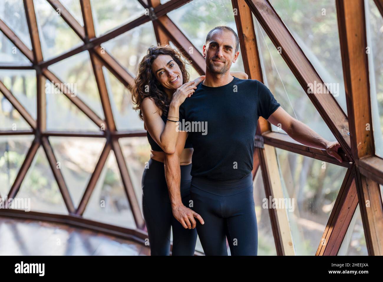 Front view of sportive couple in activewear cuddling near windows while ...