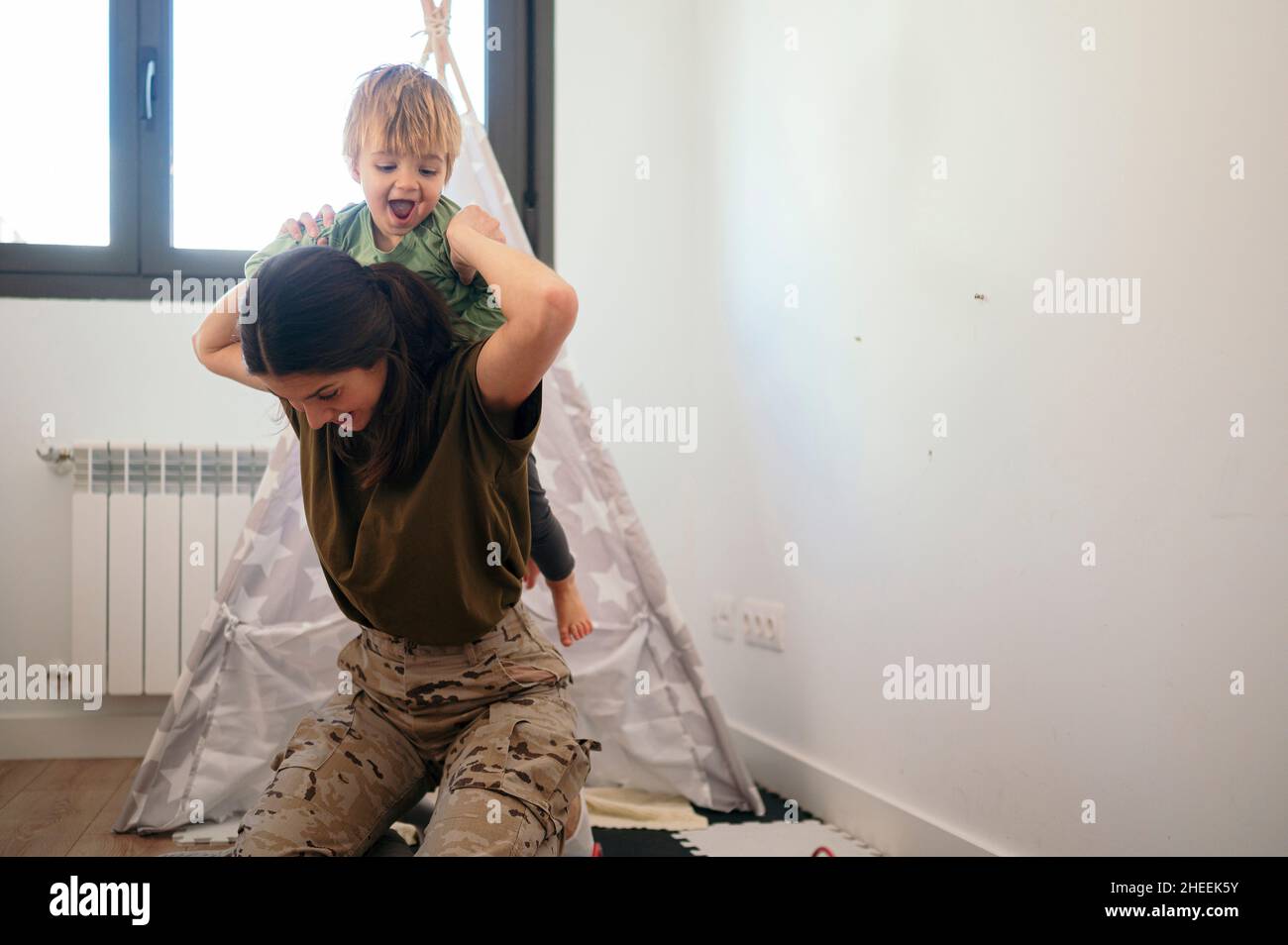 Positive military Woman in uniform giving piggyback ride to cute son ...