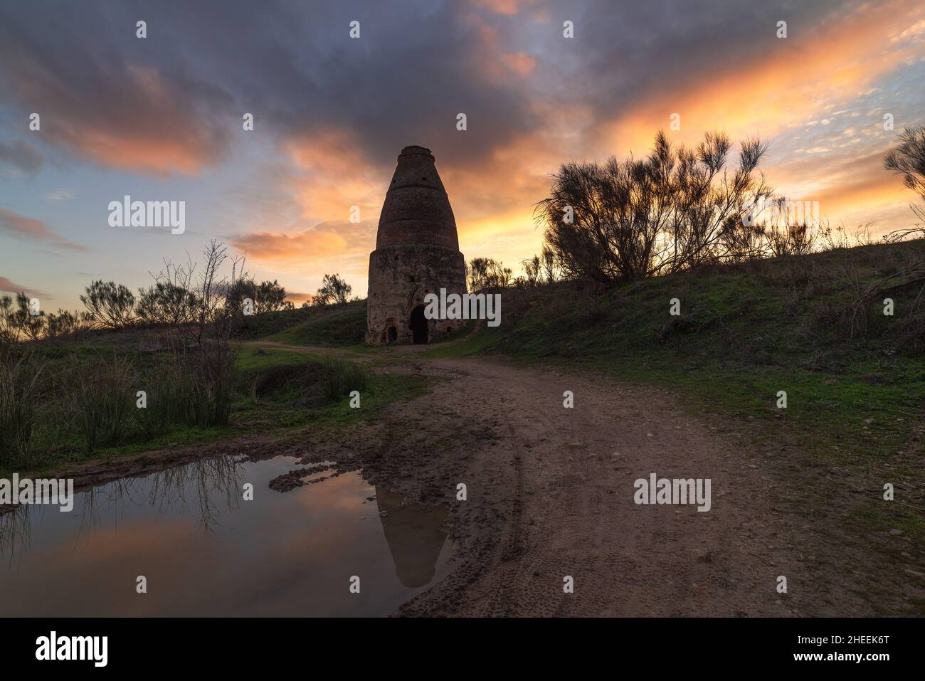 Aged lime kiln located on shore of calm reflective pond against cloudy ...