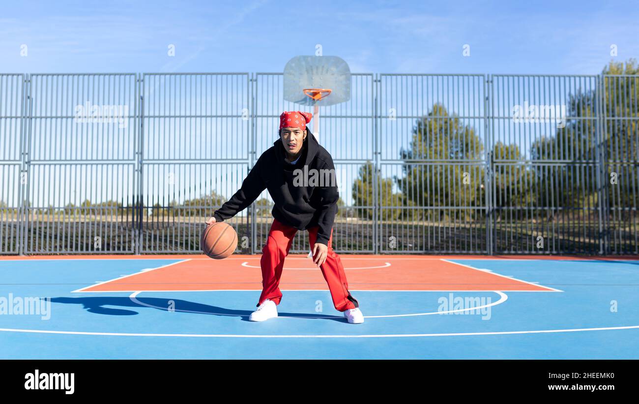 Full body of sportive Asian man in activewear dribbling ball during ...