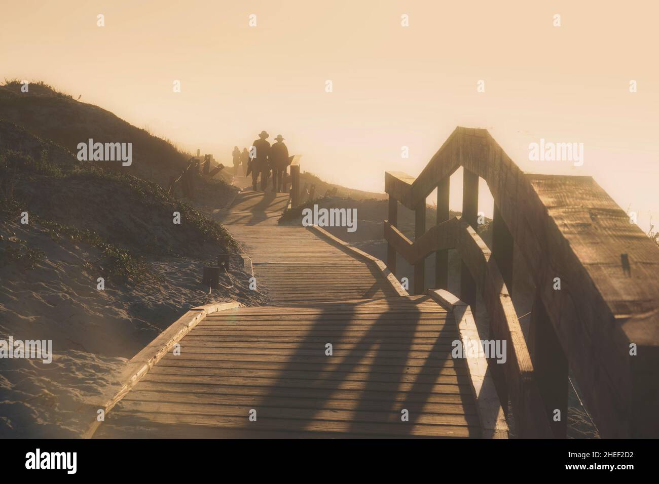 Couple stroll on the boardwalk in Pacific Grove, as the sun sets over ...