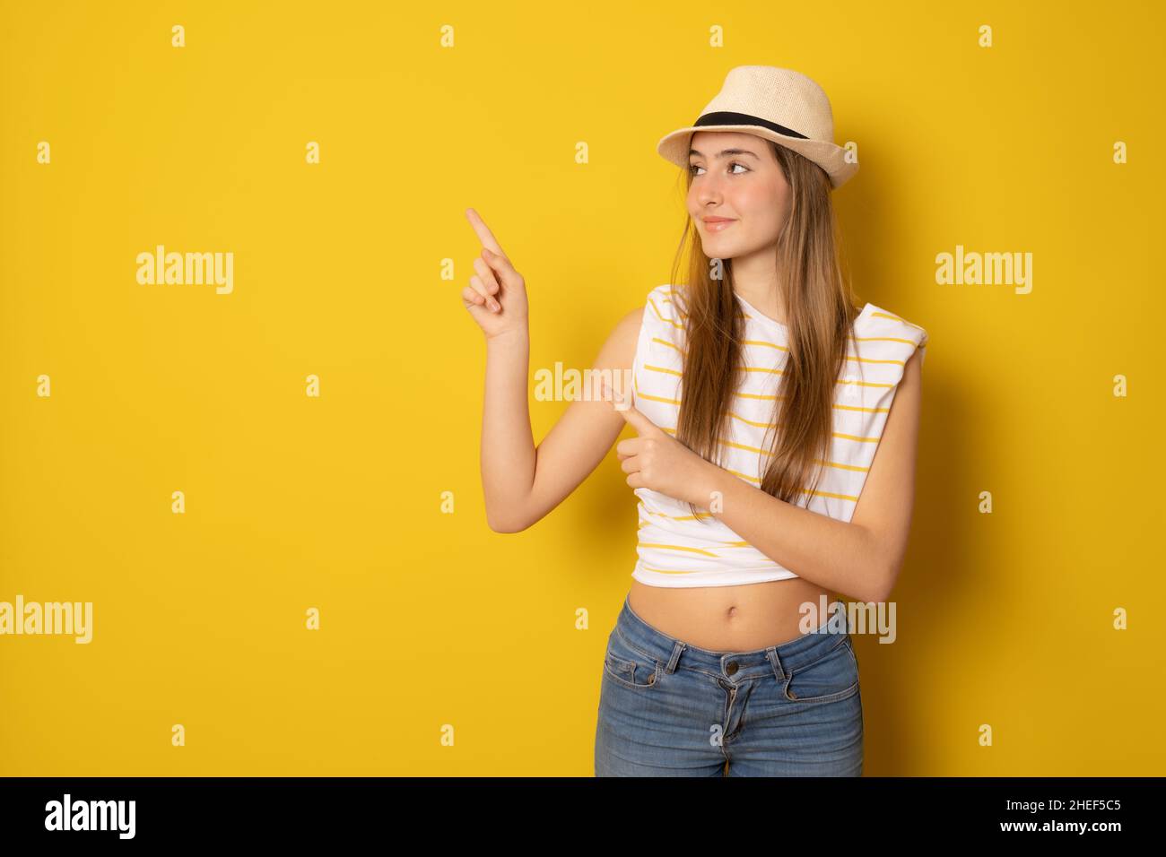 Young woman wearing straw hat pointing fingers up isolated over yellow ...